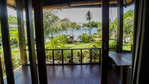 Um deck de madeira aberto com vista para um jardim tropical e um corpo de água.