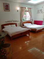 Quarto de hotel com duas camas de madeira, janela com cortinas, ar condicionado fixado na parede e um objeto decorativo na parede.