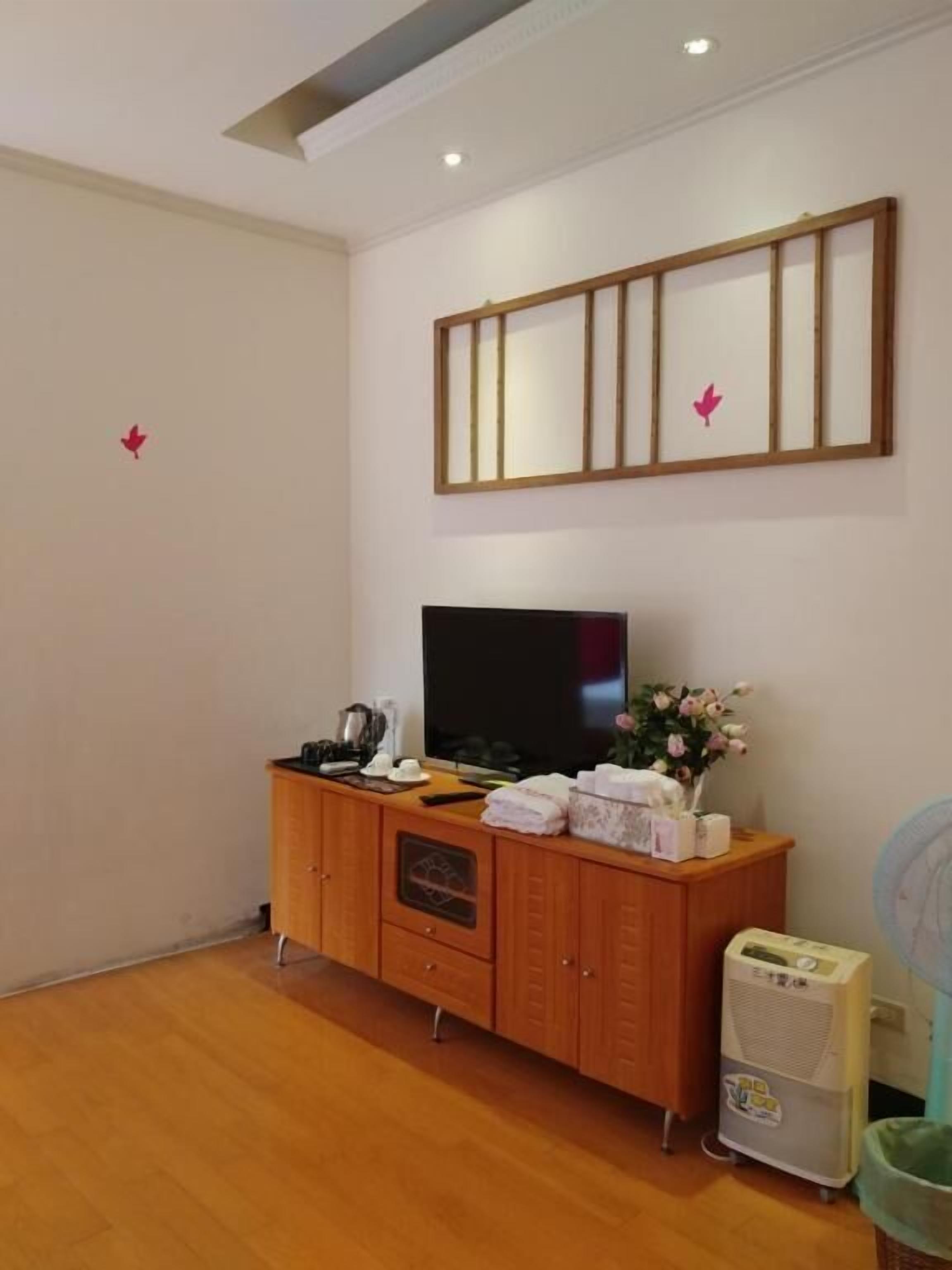 Quarto com armário de madeira, TV de tela plana, ventilador e prateleira fixada na parede.