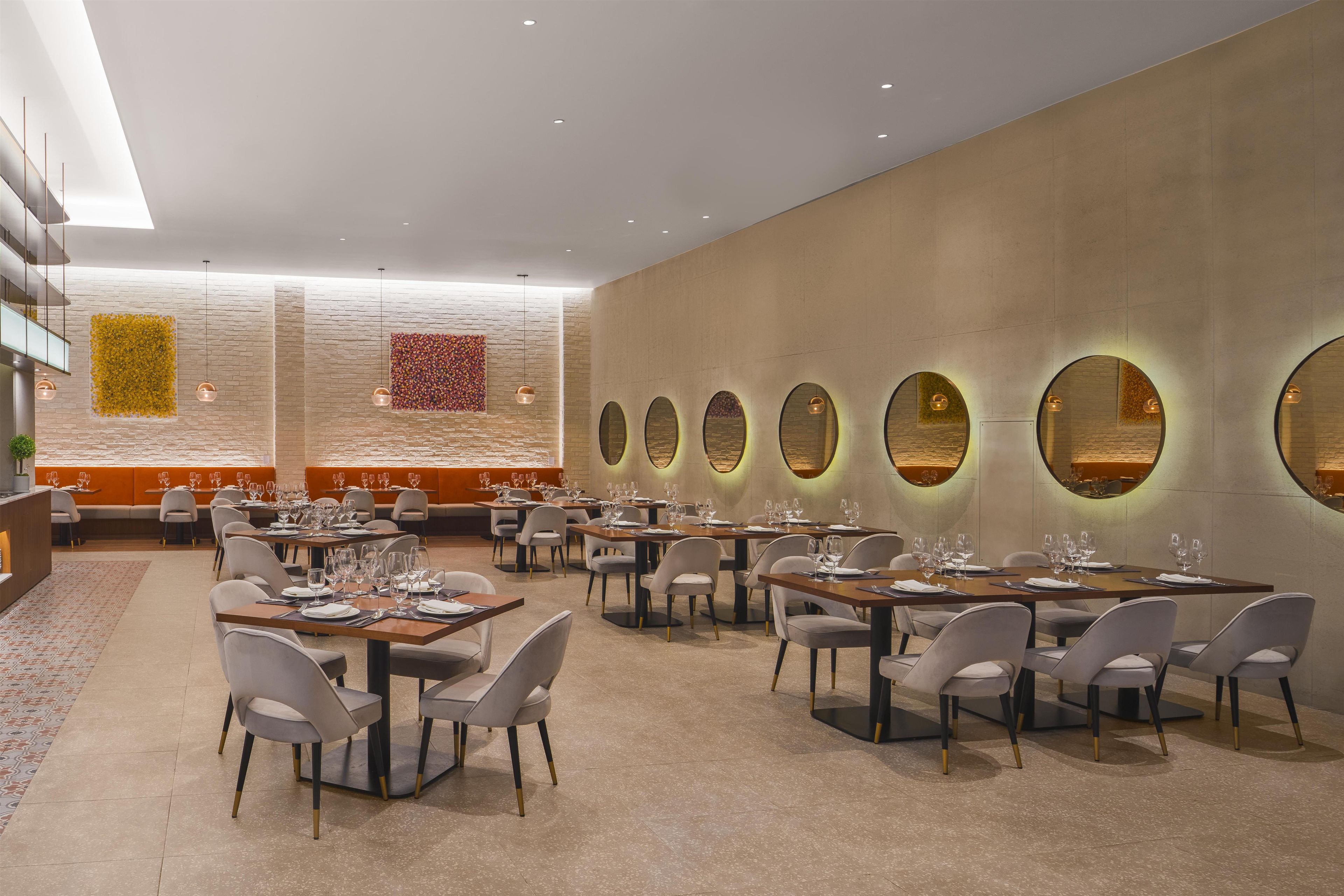 Um restaurante moderno com parede de tijolos, espelhos redondos e área de estar com mesas e cadeiras.