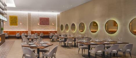 Um restaurante moderno com parede de tijolos, espelhos redondos e área de estar com mesas e cadeiras.