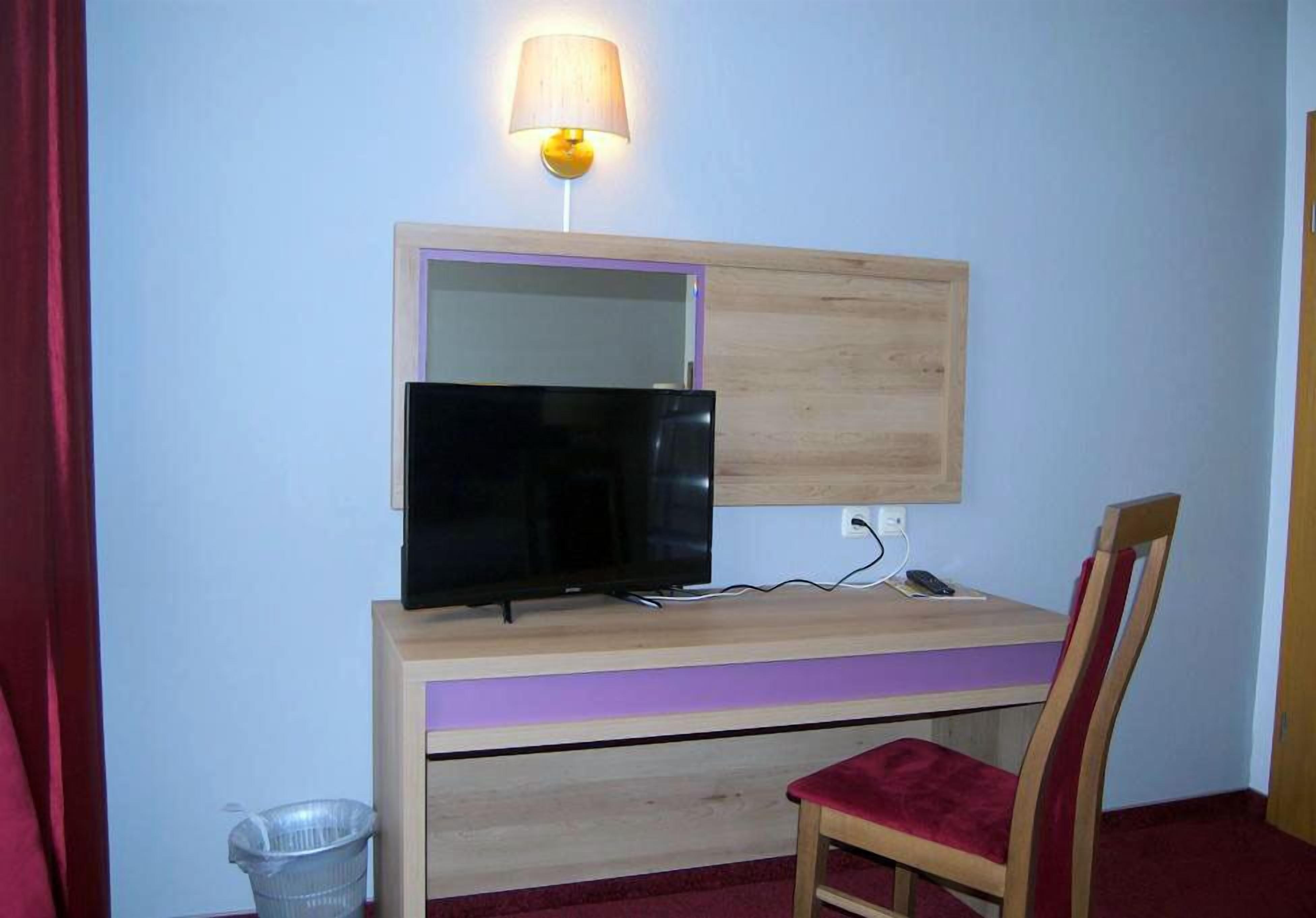 Um quarto pequeno com uma escrivaninha de madeira, televisão, luminária e uma cadeira.