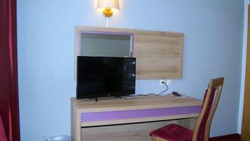 Um quarto pequeno com uma escrivaninha de madeira, televisão, luminária e uma cadeira.