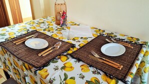 Uma mesa de jantar com toalha de mesa estampada com limões, dois jogos americanos quadrados e talheres.