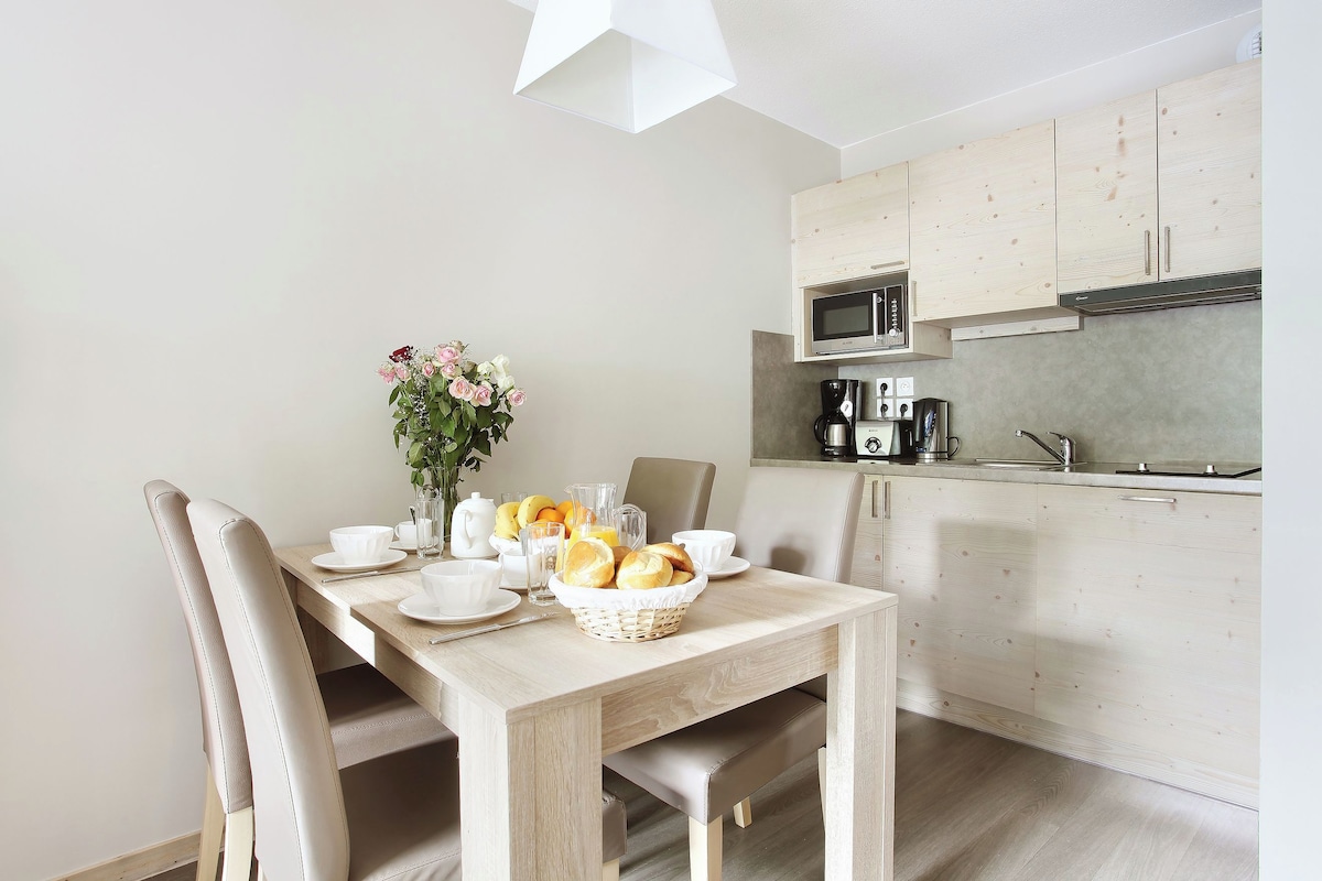 Uma área de refeições com uma mesa de madeira posta para o café da manhã, incluindo pão, frutas e um vaso de flores.