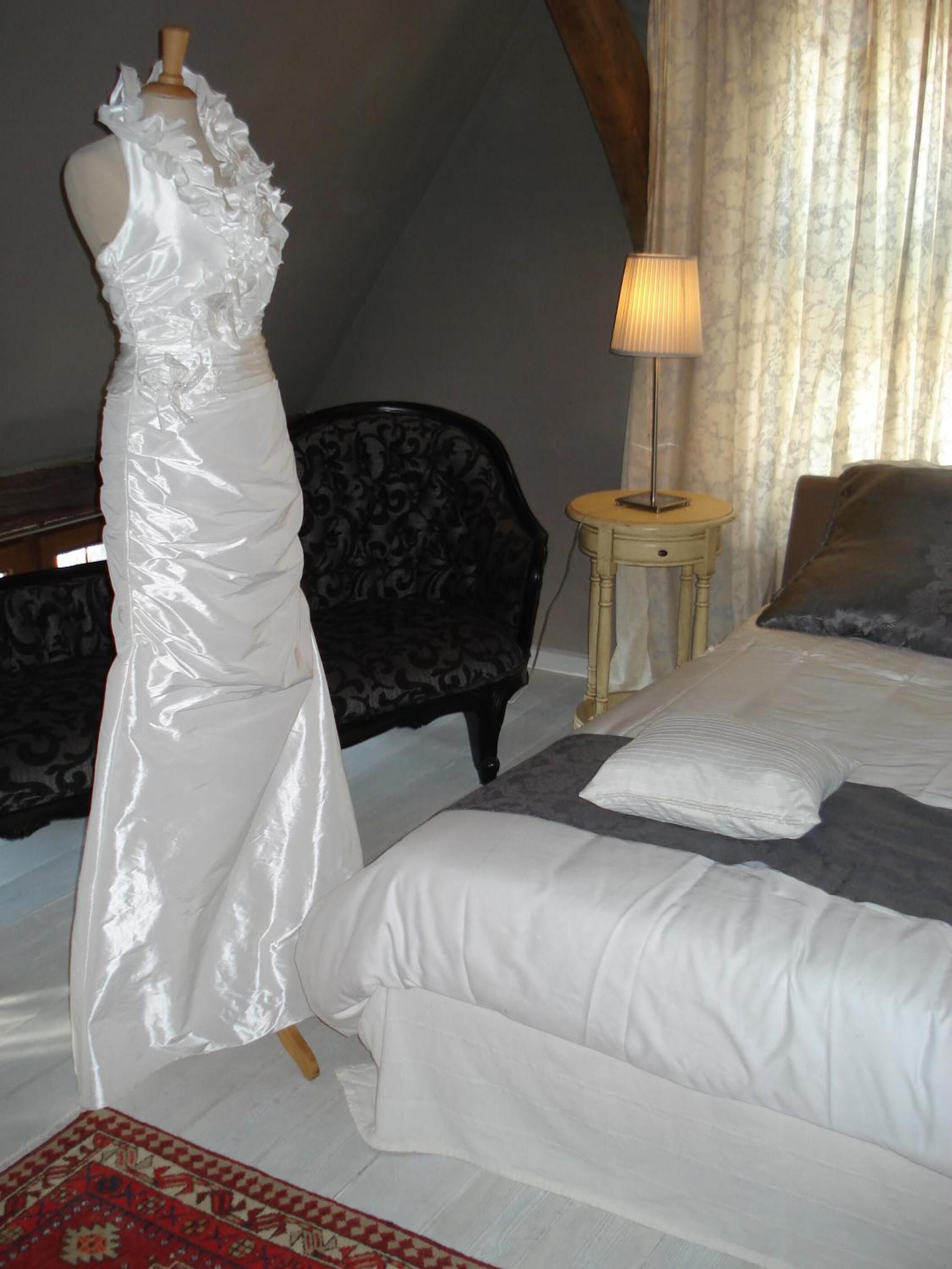 Um quarto com uma cama, uma luminária, uma cadeira e um vestido em um manequim.