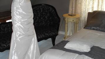 Um quarto com uma cama, uma luminária, uma cadeira e um vestido em um manequim.