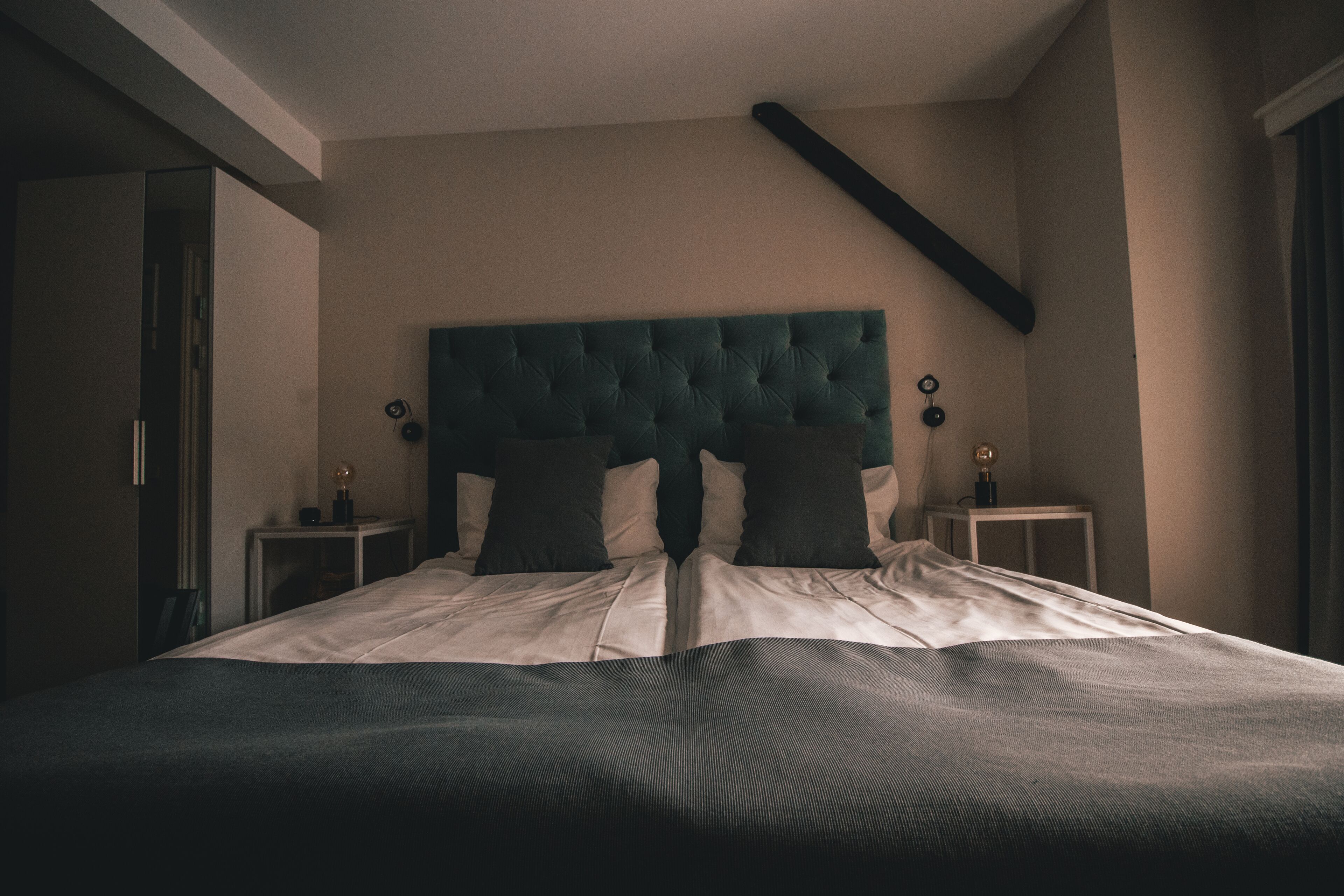 Quarto com cabeceira estofada, duas mesas de cabeceira com luminárias e uma cama grande com cobertor escuro.