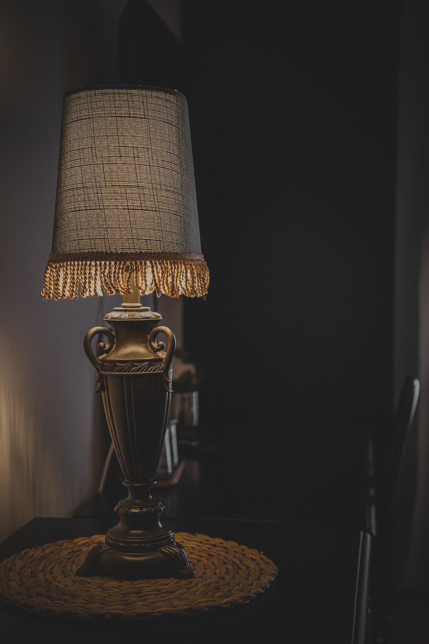 Uma luminária de mesa com cúpula texturizada e base trançada, sobre uma superfície escura.