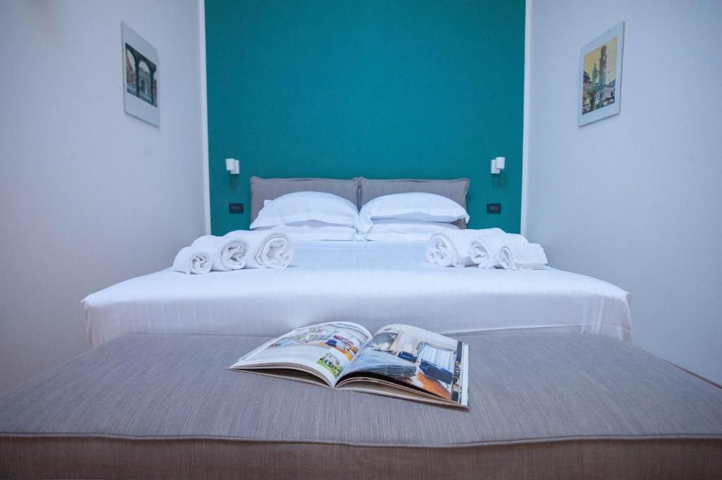 Uma cama bem arrumada com roupa de cama e almofadas brancas, e uma revista sobre a cama, com paredes cor de verde-água.