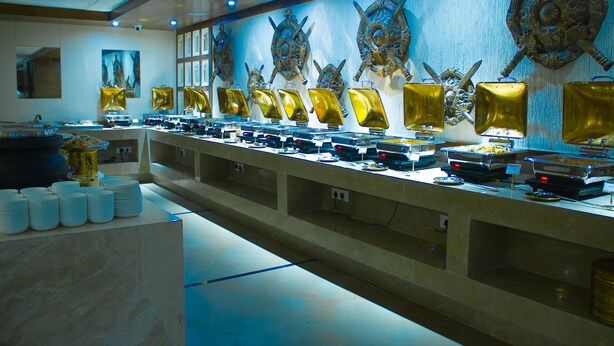 Disposição de buffet com diversas estações de comida, balcão de mármore e arte decorativa na parede.