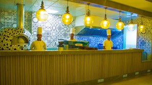 Interior de restaurante com parede estampada, balcão de madeira e luminárias pendentes.