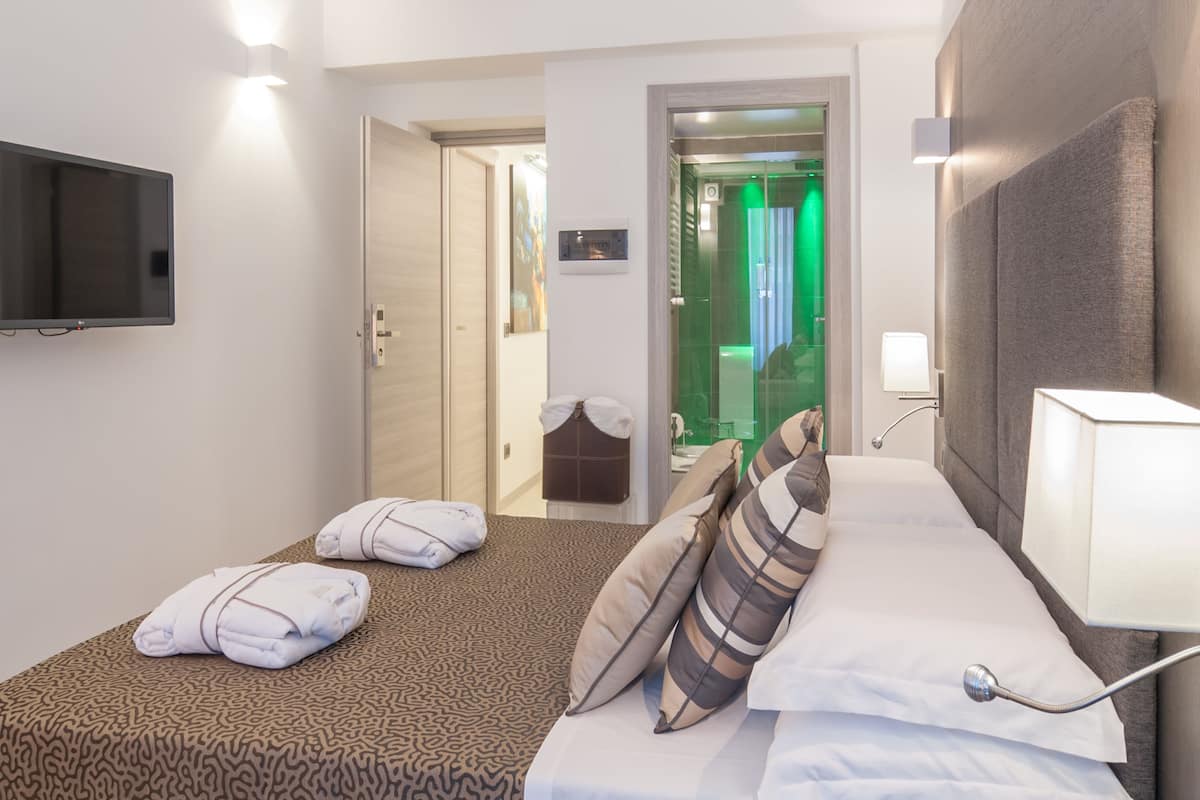 Quarto de hotel com cama, televisão, banheiro com chuveiro e porta-toalhas.