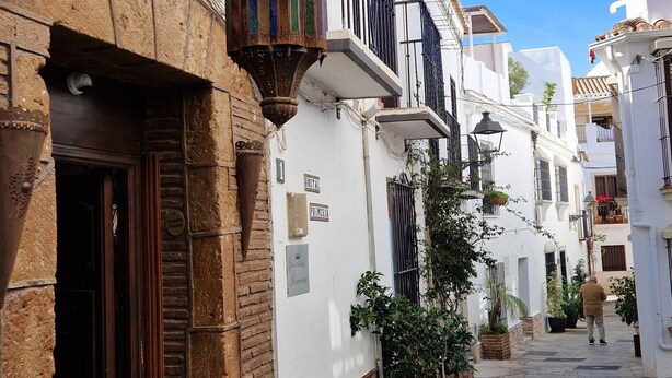 Uma rua estreita com edifícios brancos, uma porta de madeira e um vaso de planta.