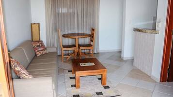 Uma sala de estar com sofá, duas cadeiras de madeira, uma mesa de centro e um tapete pequeno.
