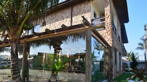 Um edifício de pedra com varanda, pérgola com cobertura de vidro e uma palmeira.