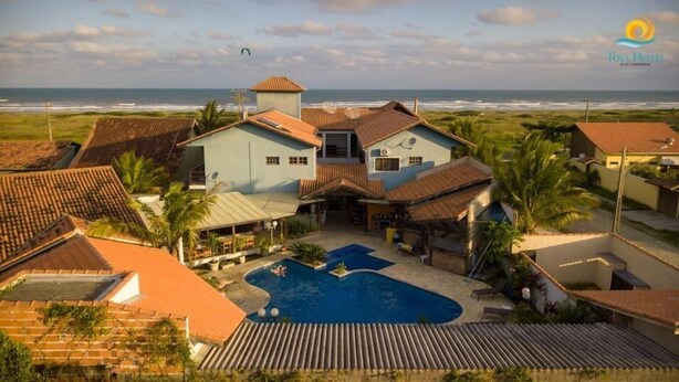 Um resort com piscina, vista para a praia e vários edifícios com telhados em cerâmica.