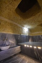 Um quarto de spa com parede de pedra, banheira de mármore e pia de pedra.