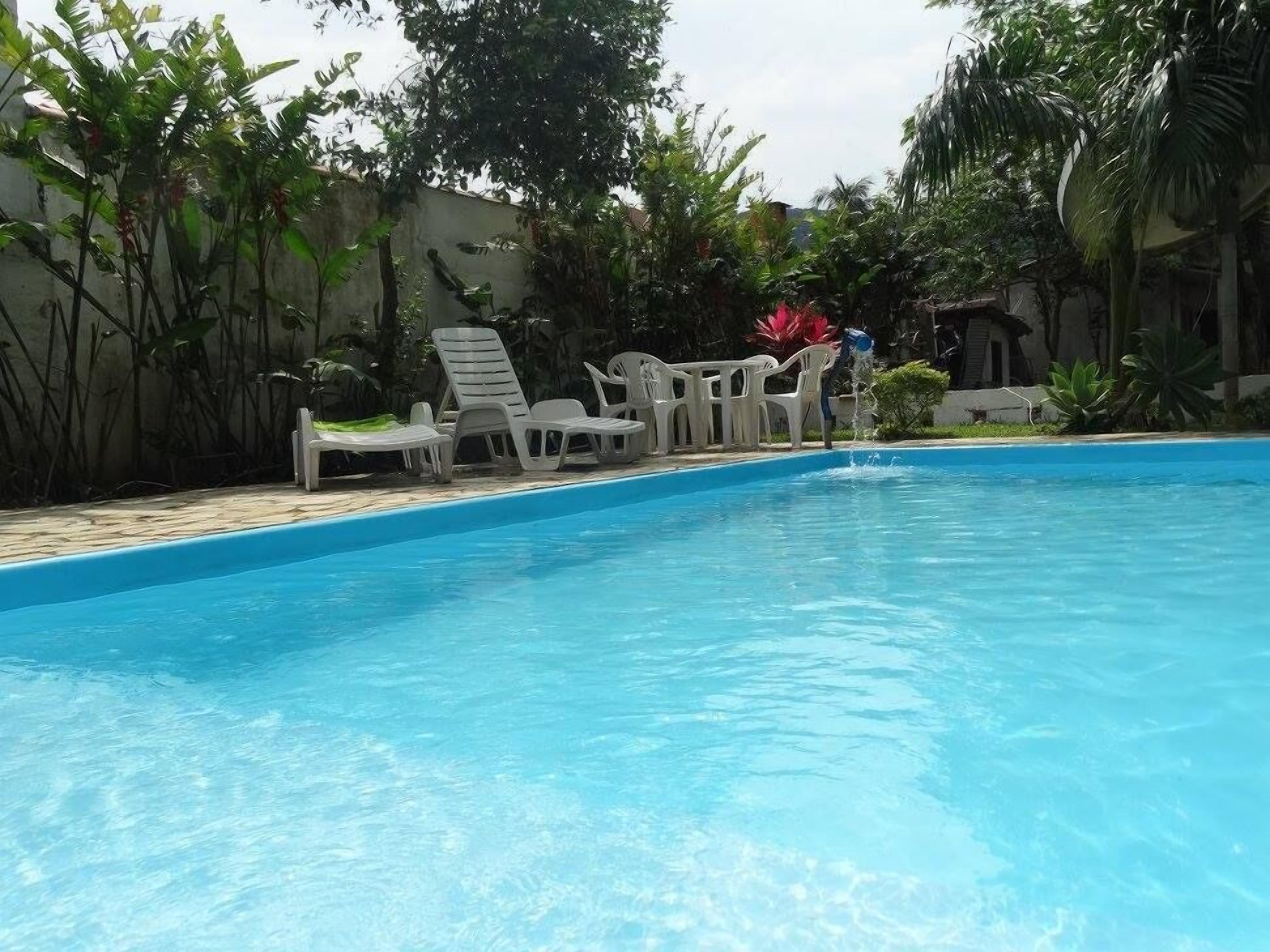 Piscina com água azul cristalina, rodeada por espreguiçadeiras brancas e plantas tropicais.