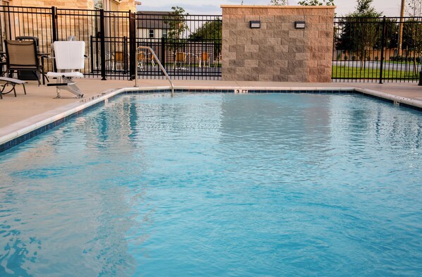 Piscina retangular com escada de metal, rodeada por um muro de pedra e cerca de metal preto.
