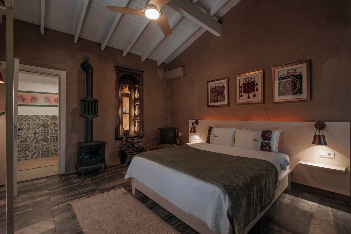 Quarto com cama, lareira, ventoinha no teto e quadros nas paredes.