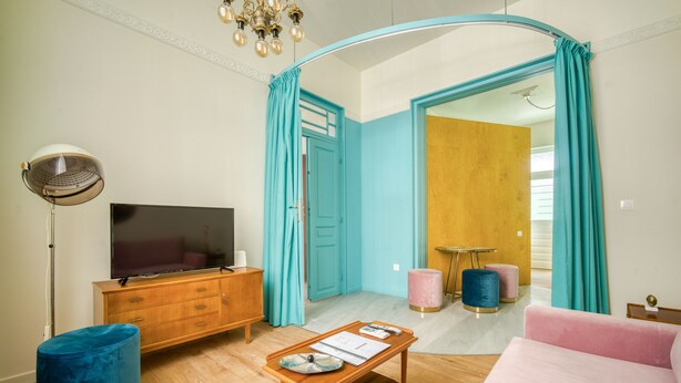 Uma sala de estar moderna com televisão, móveis de madeira, um banquinho azul e cortinas verde-água.