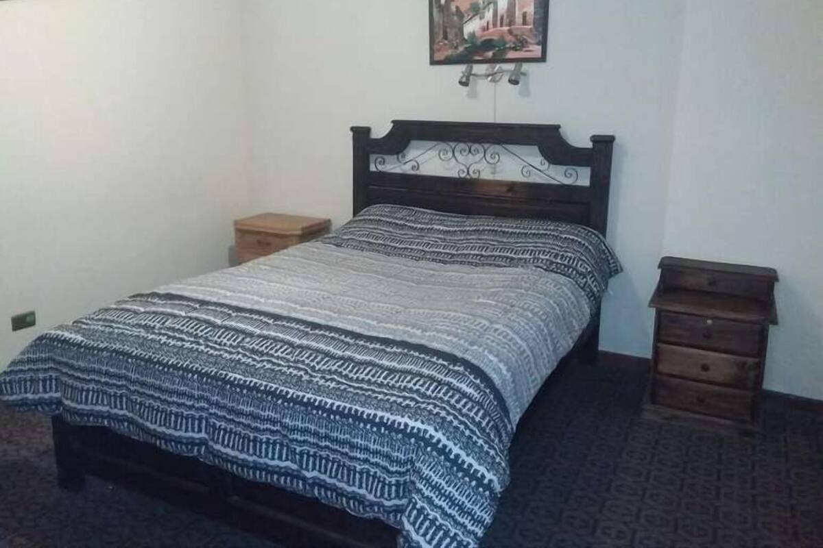 Quarto com cama, mesa de cabeceira, cômoda e um quadro na parede.