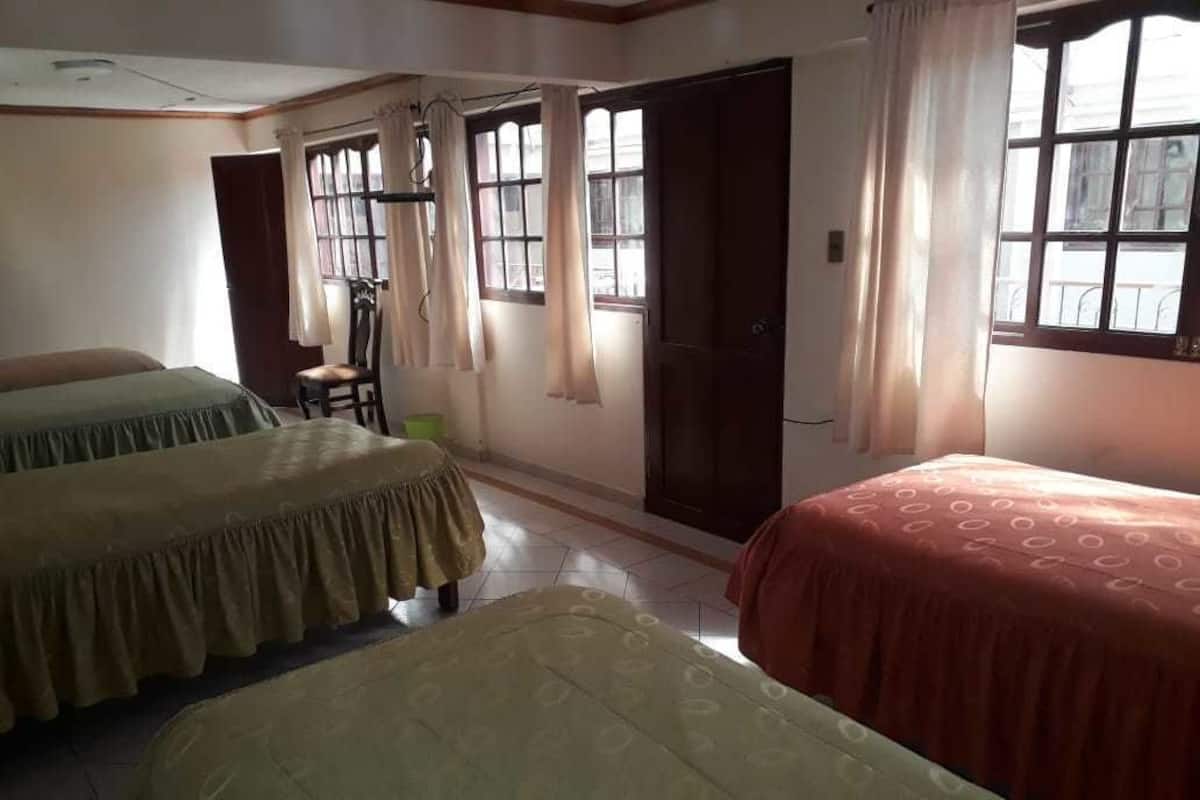 Quarto com duas camas, uma cadeira e janela com cortinas.