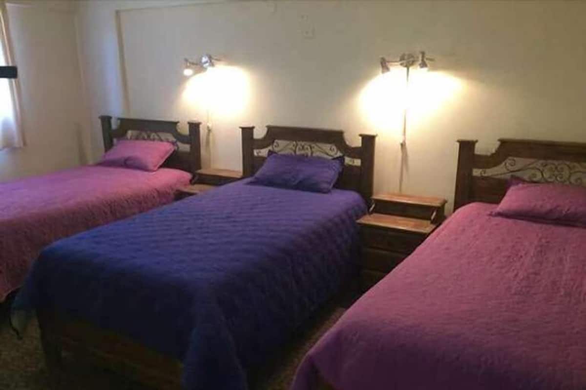 Quarto com três camas de solteiro, cada uma com cabeceira e luminárias de cabeceira.
