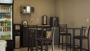 Uma pequena cozinha compacta com micro-ondas, cafeteira e geladeira. Quatro cadeiras ao redor de uma mesa.