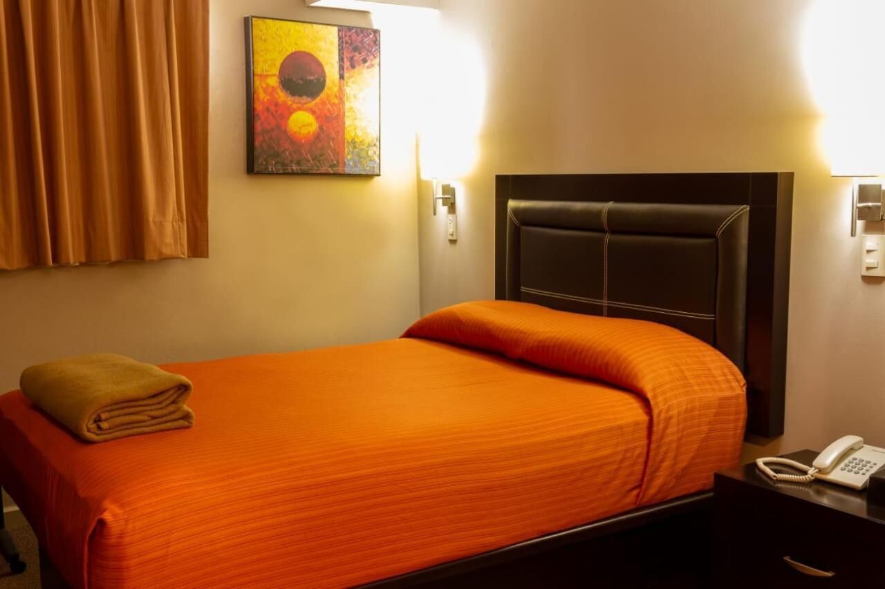 Quarto de hotel com cama, mesa de cabeceira com telefone e um quadro na parede.