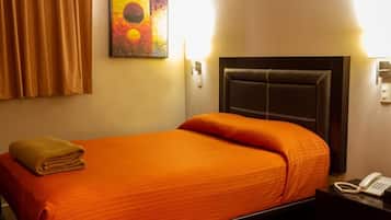 Quarto de hotel com cama, mesa de cabeceira com telefone e um quadro na parede.