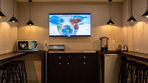 Uma cozinha moderna com uma televisão grande, banquetas de bar e uma máquina de café.