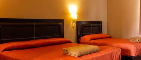 Quarto de hotel com duas camas, cada uma com cabeceira e uma cama com travesseiro.