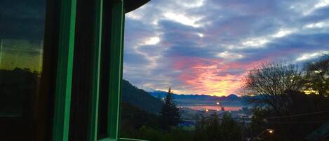 Uma varanda com vista para um pôr do sol sobre montanhas e um corpo d'água.