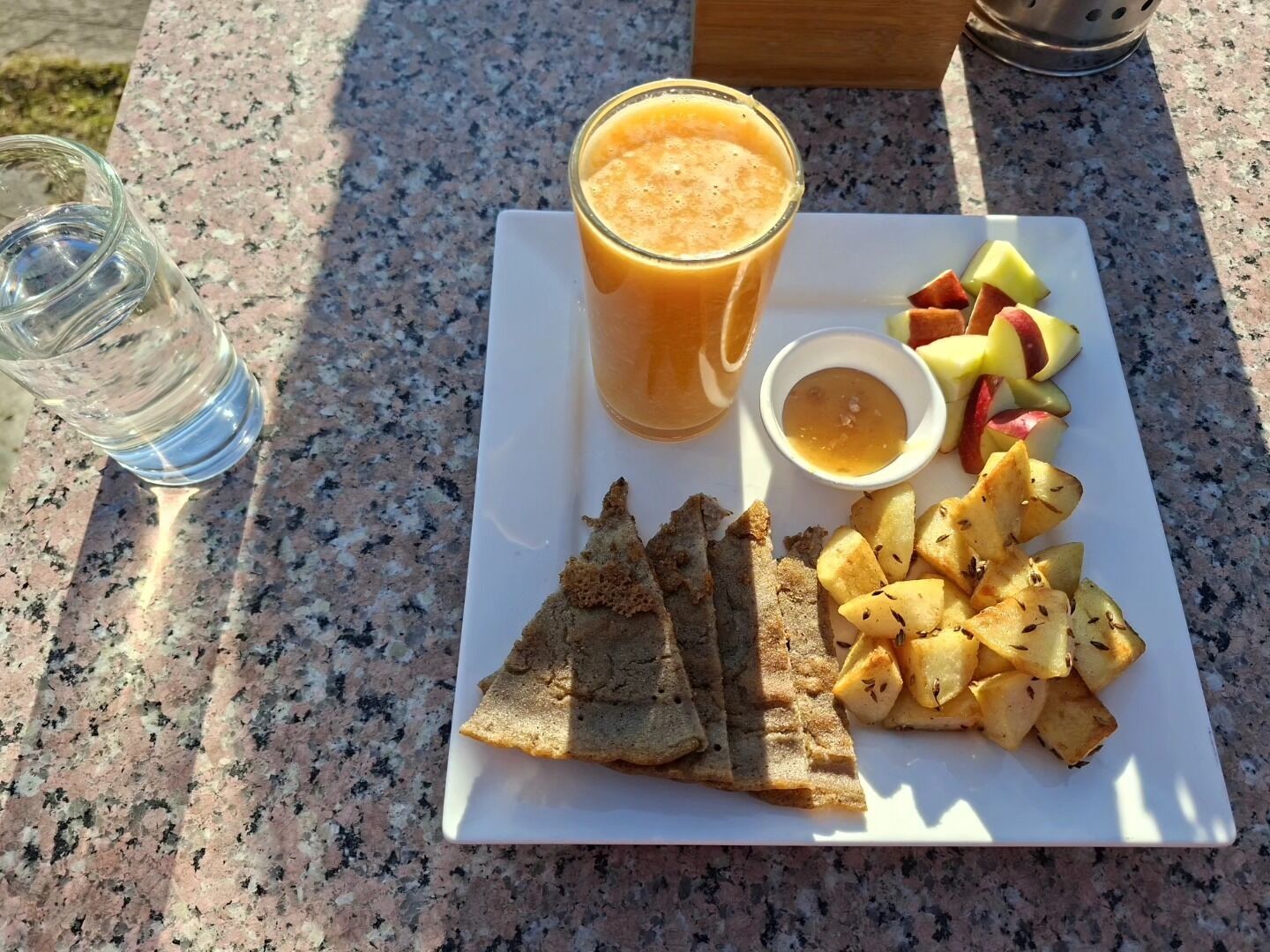 Um prato com um smoothie, fatias de maçã, batatas fritas e bolachas sobre uma mesa de granito.