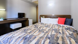 Quarto de hotel com uma cama, escrivaninha, televisão e ar condicionado.