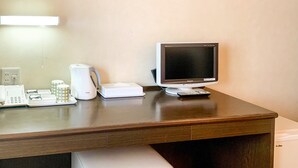 Quarto de hotel com uma secretária de madeira, chaleira branca, televisão Panasonic, comando remoto e telefone.
