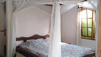 Quarto com cama sob um dossel branco, janela com cortinas e chão de azulejos.
