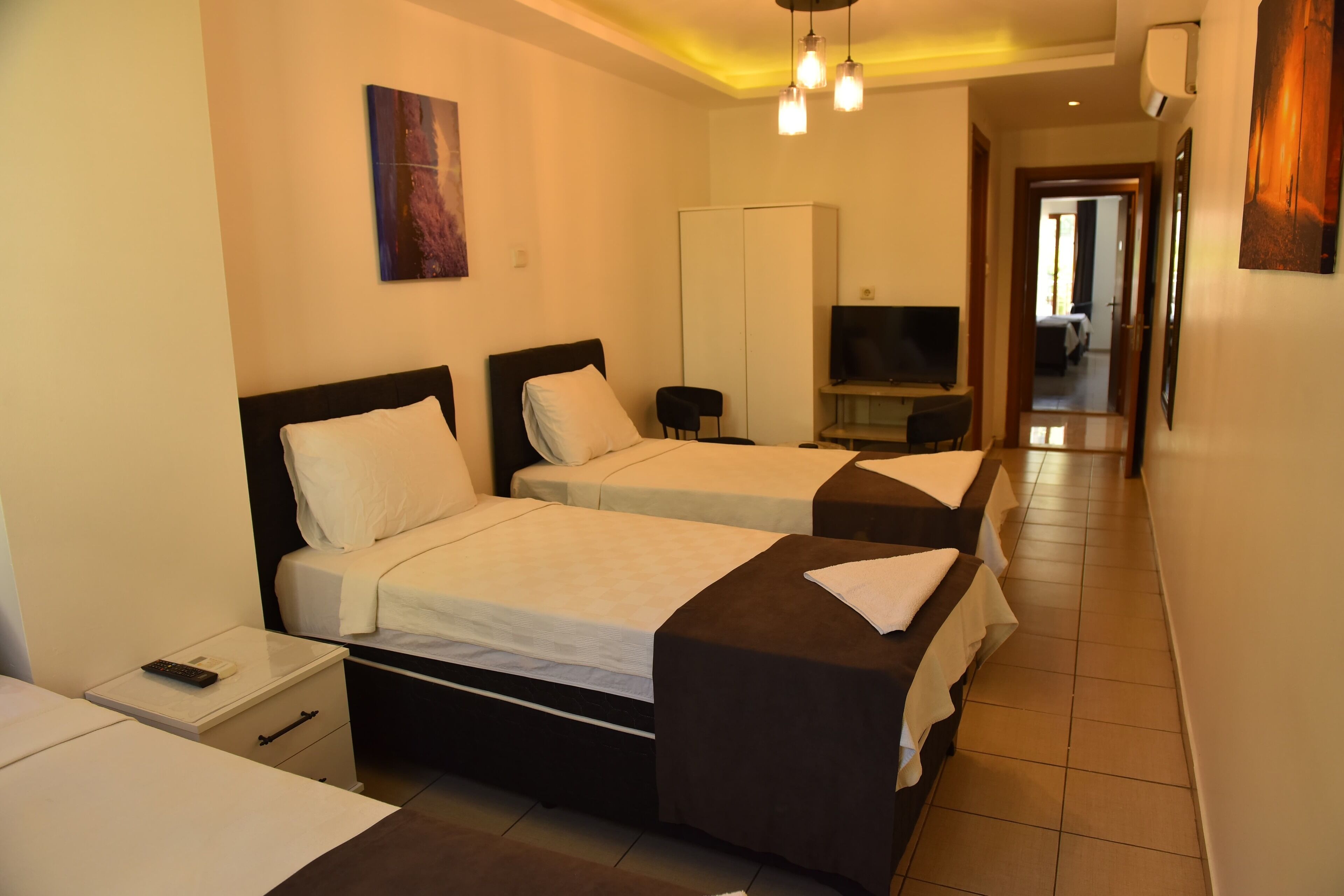 Quarto de hotel com duas camas, televisão, guarda-roupa e corredor que dá para outro quarto.