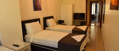 Quarto de hotel com duas camas, televisão, guarda-roupa e corredor que dá para outro quarto.