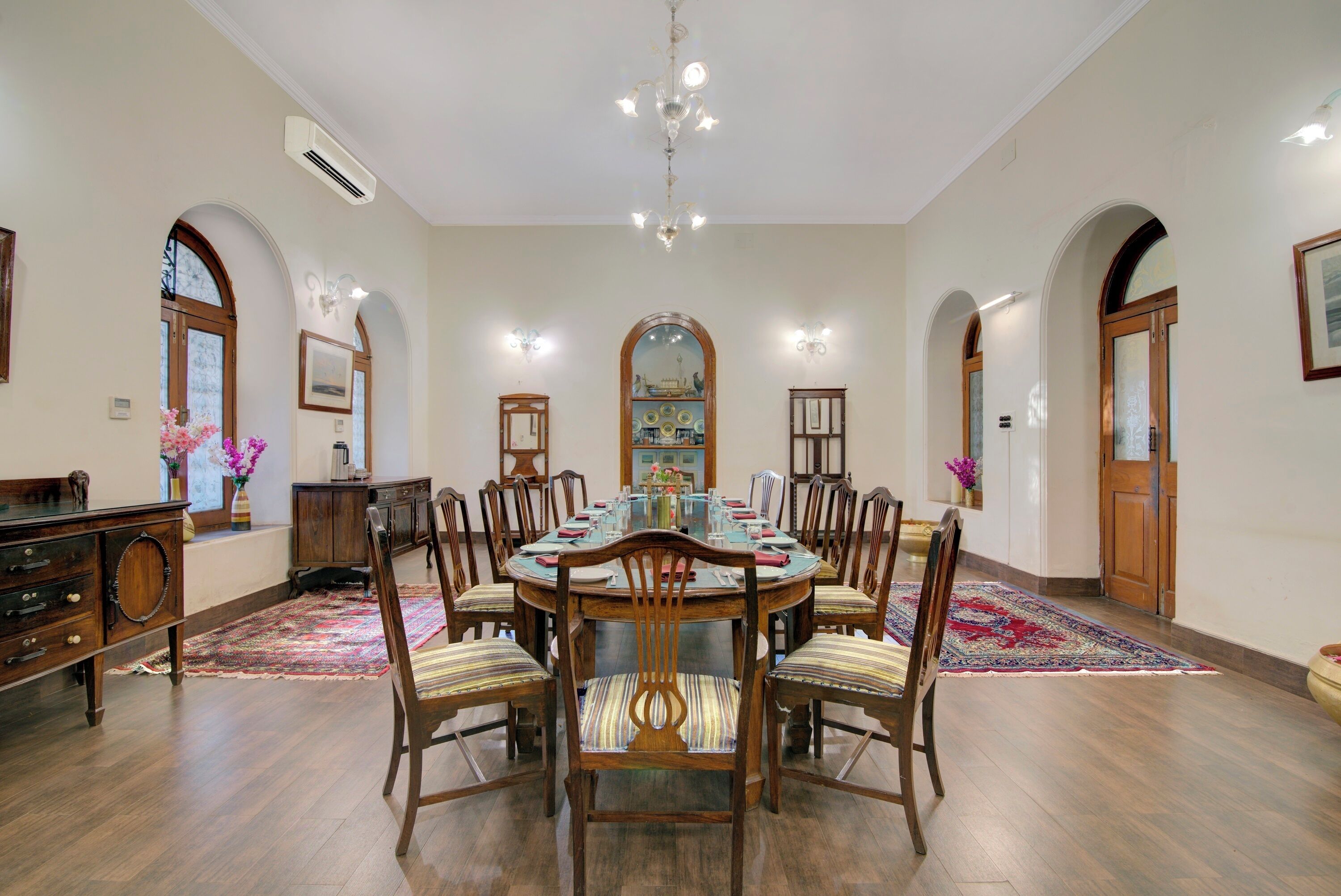 Uma sala de jantar com uma mesa redonda, cadeiras de madeira e um candelabro.