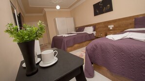 Quarto de hotel com duas camas, uma mesinha com xícara e pires, um vaso de planta e um quadro na parede.