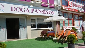 Edifício com placa indicando "DOĞA PANSIYON" e área externa com mesas e guarda-sóis.