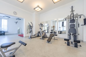 Uma academia com diversos equipamentos de exercício, um relógio na parede e uma janela com persianas.