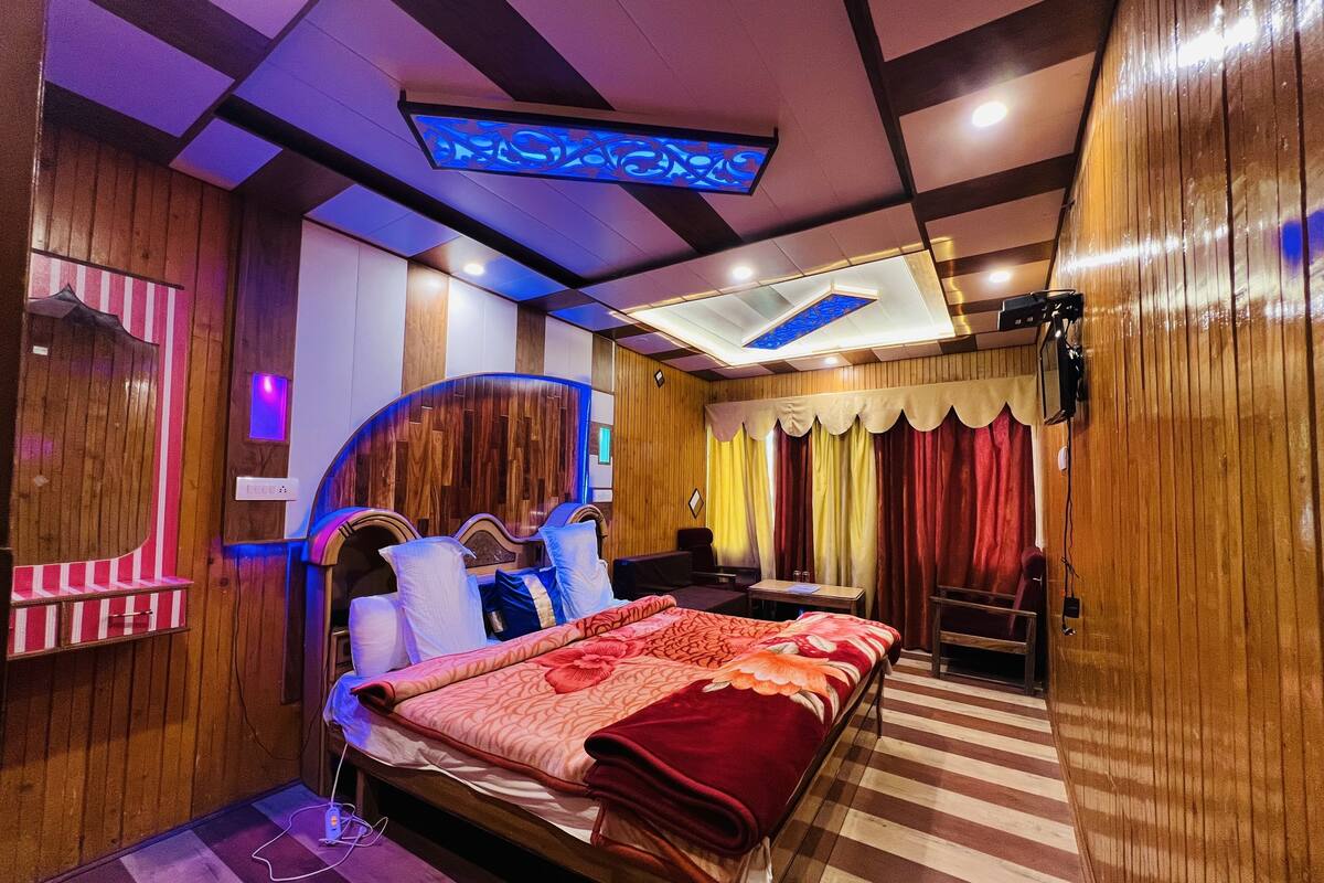 Quarto moderno com cabeceira de madeira, cama grande com colcha florida vermelha, mesa de cabeceira e luminária no teto.
