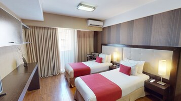 Quarto de hotel com duas camas, uma escrivaninha, uma cadeira, uma televisão e aparelho de ar condicionado.