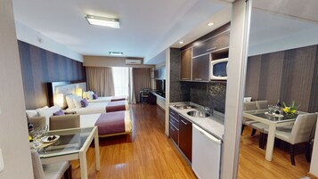 Quarto de hotel moderno com cozinha compacta, área de refeições e sala de estar com sofá e cadeiras.