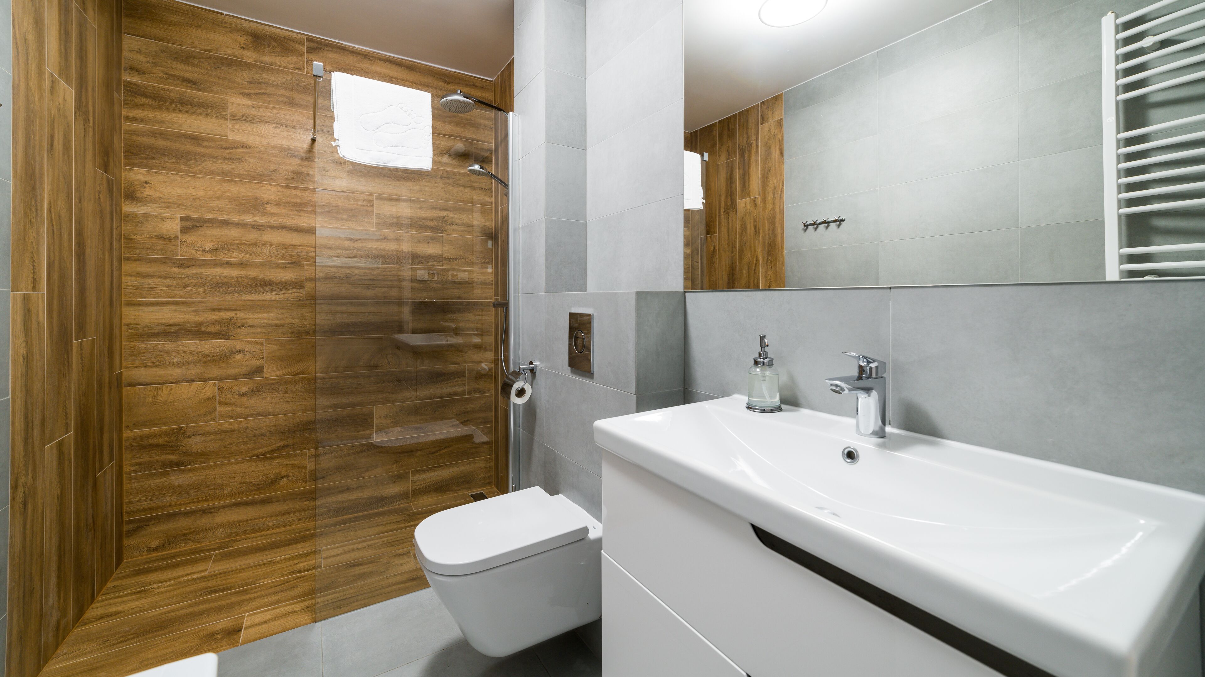 Uma casa de banho moderna com cabine de chuveiro em madeira, lavatório branco com torneira cromada e sanita.