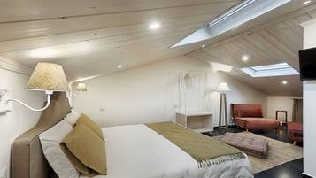 Quarto com cama, luminária de cabeceira, mesinha, cadeira vermelha e televisão na parede.